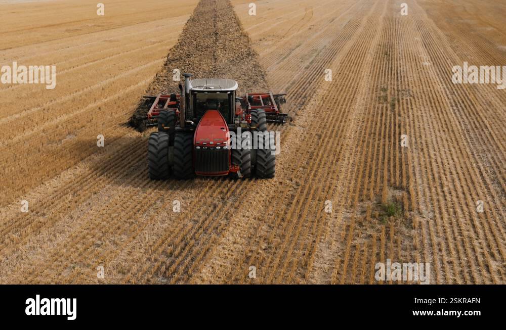Disking the field. Big red Tractor cultivating land of Disc Harrow ...