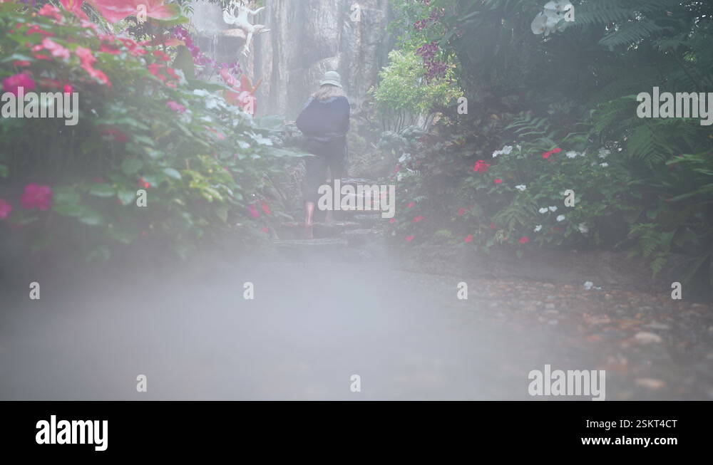 Woman in blue shawl walking barefoot on wet garden path to waterfall ...