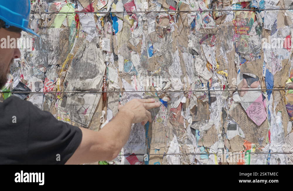 Worker controls compact bale of paper at recycling facility, static ...