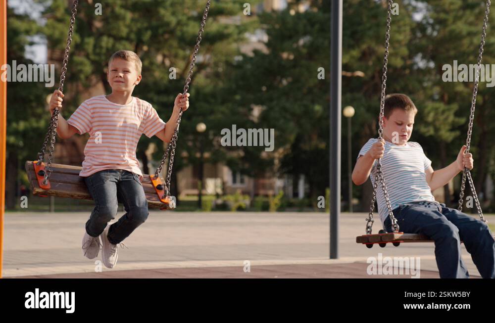 Boys swing on swings, friends play in childrens park. Children swinging on swing Stock Video ...