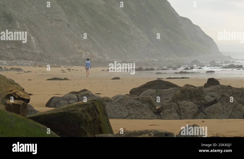 Relaxed mindfull man walking lonely at a deserted coast with rocks ...