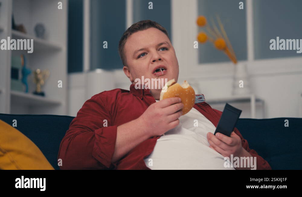 Lazy young man eating junk food and watching tv on couch, unhealthy ...