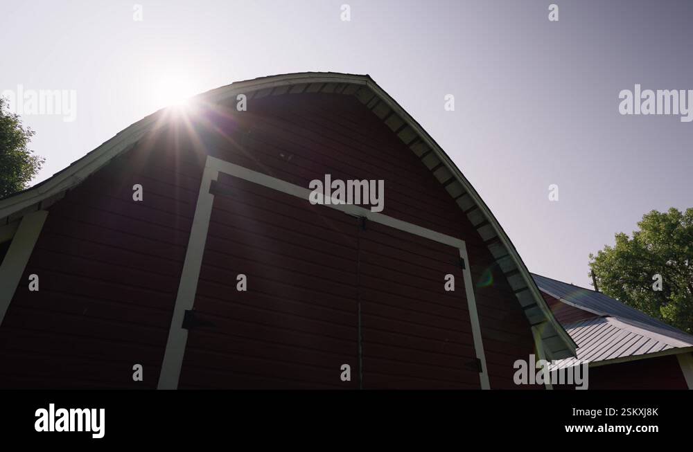 a red barn on a farm with the sun flaring behind the roof of the barn ...