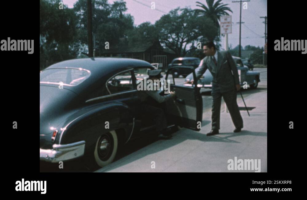 1950s: Car pulls up to curb. Police officer and young man get out of ...
