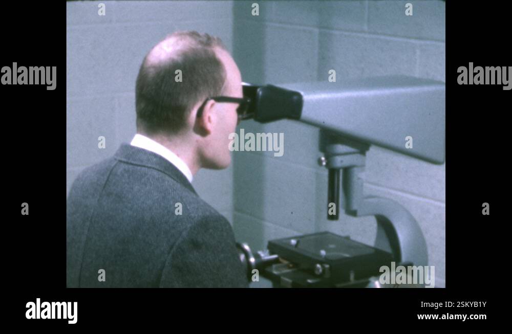 1960s: A man takes notes and looks through pair of lenses, turning dial ...
