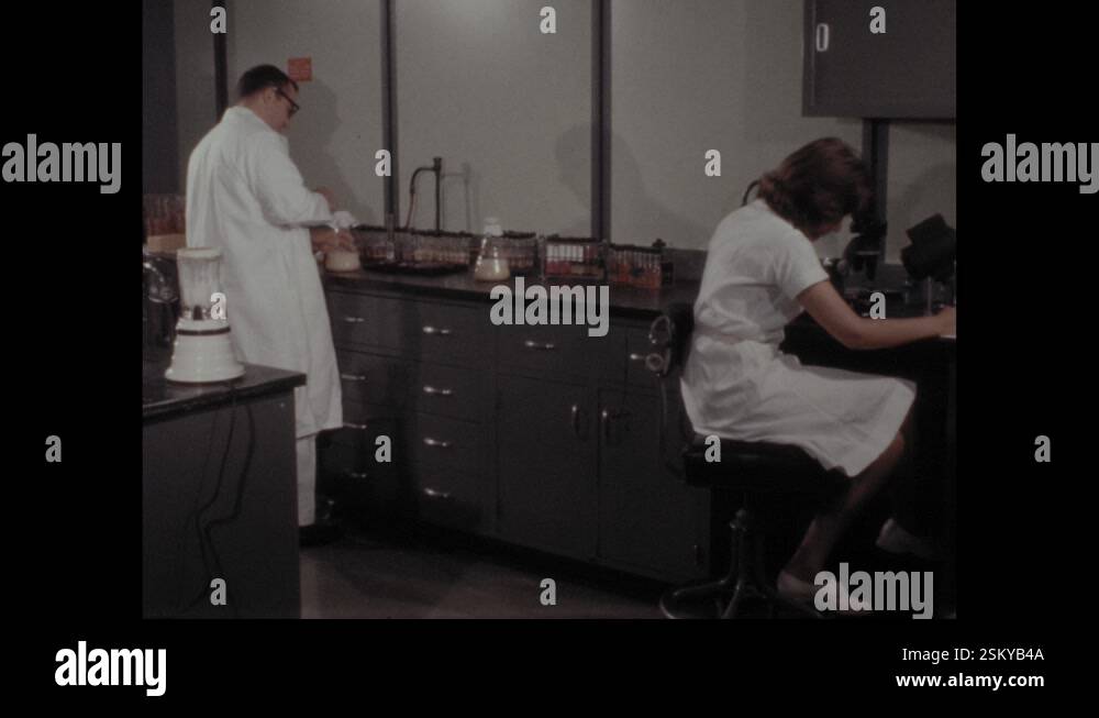 1960s: Man and woman work in medical laboratory. Man lights Bunsen ...