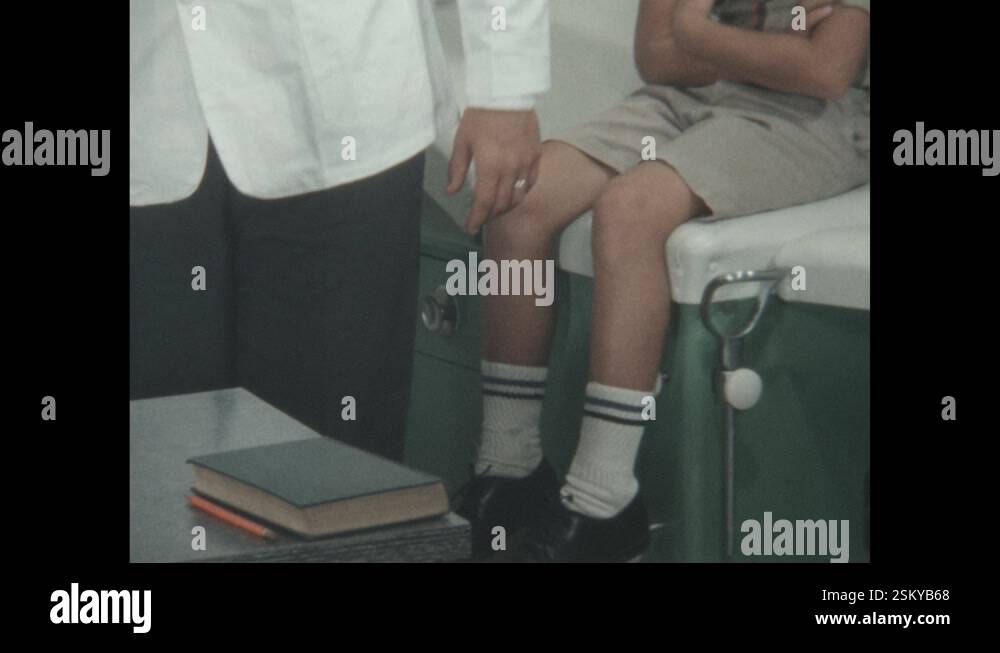 1960s: Doctor hits boy's knee with hammer during medical exam. Boy sits ...