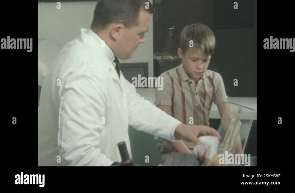 1960s: Doctor shines light into boy's eye at desk in examination room ...