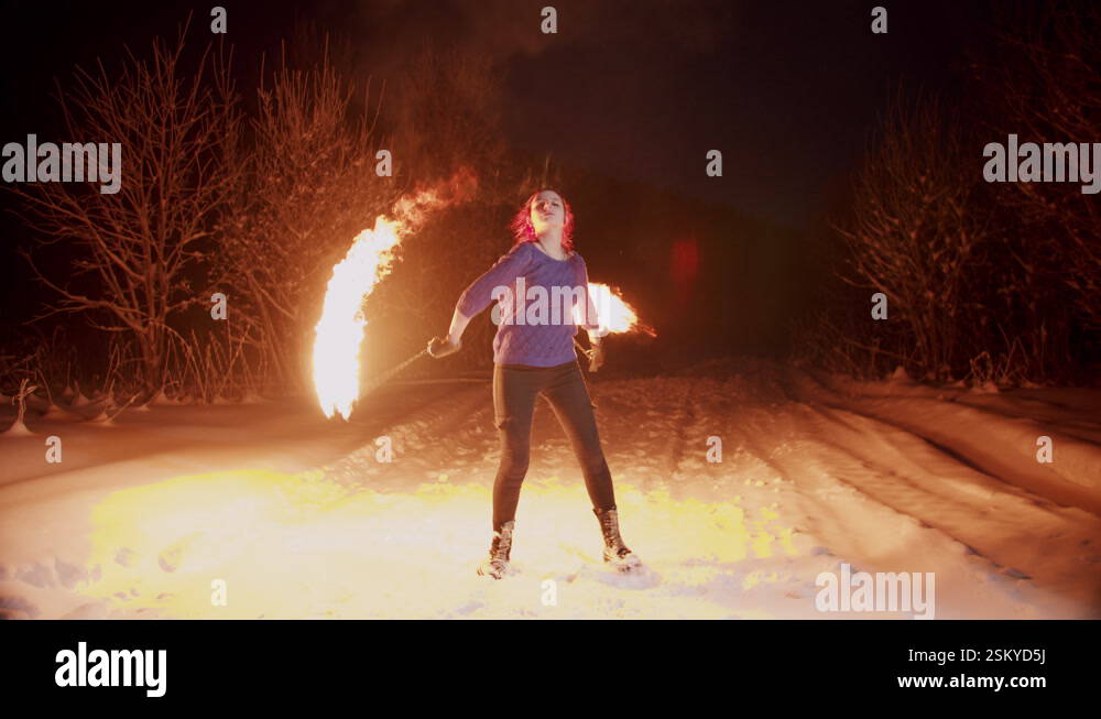 Girl in blue jacket spins fire staff poi on chains at night in the ...