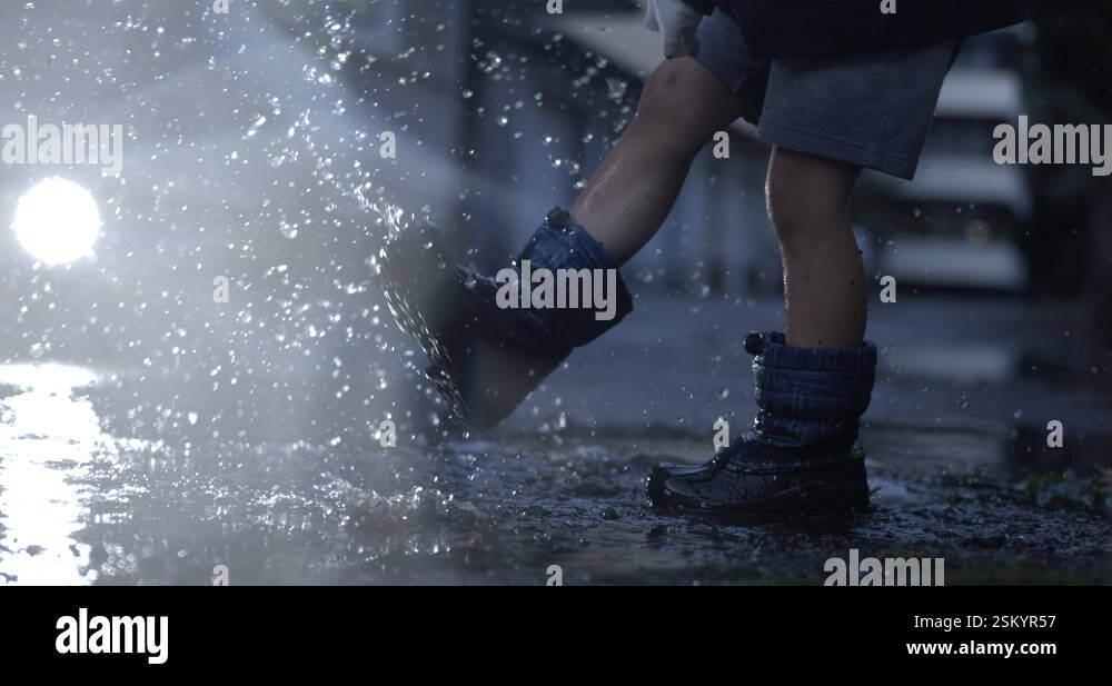 Carefree kid playing with water puddle in street kicking and splashing ...
