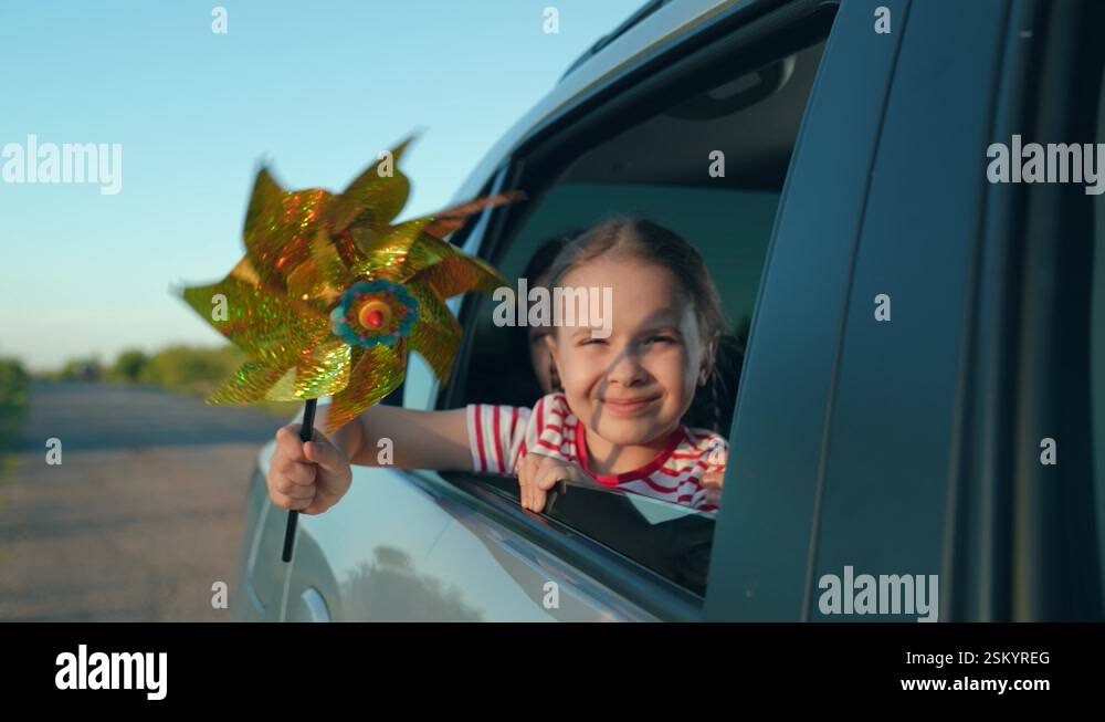 Little girl holds rotating windmill out of car window driving across ...