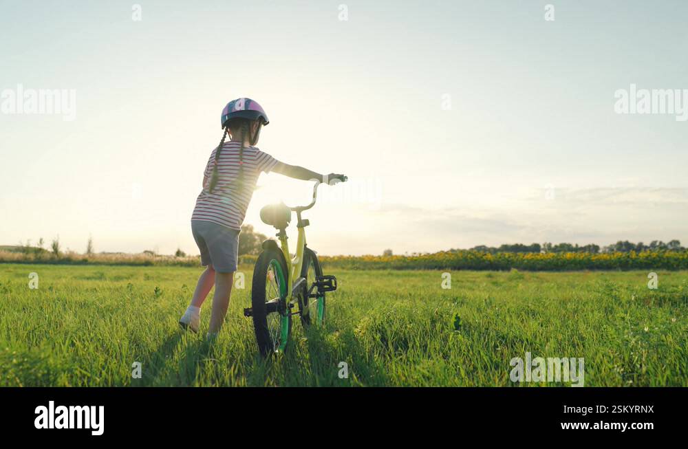 Cute little girl wearing helmet walks pulling bicycle across summer ...