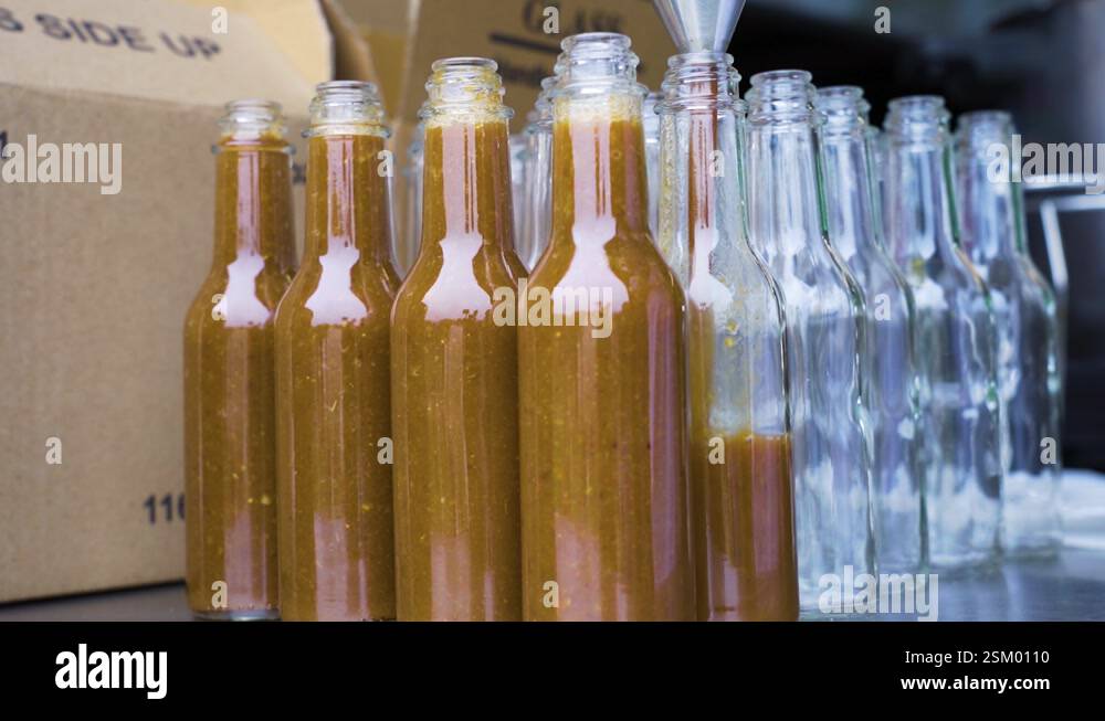 Filling up Cayenne chilli sauce into glass bottles with metal funnel ...