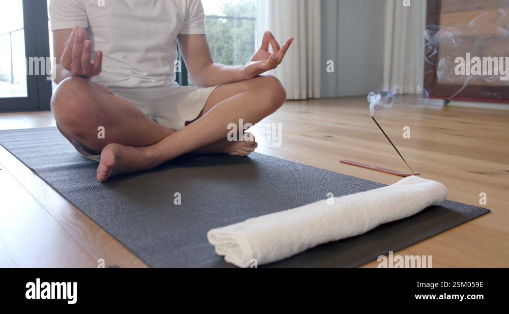 Midsection of biracial man doing yoga and meditating at home, slow ...