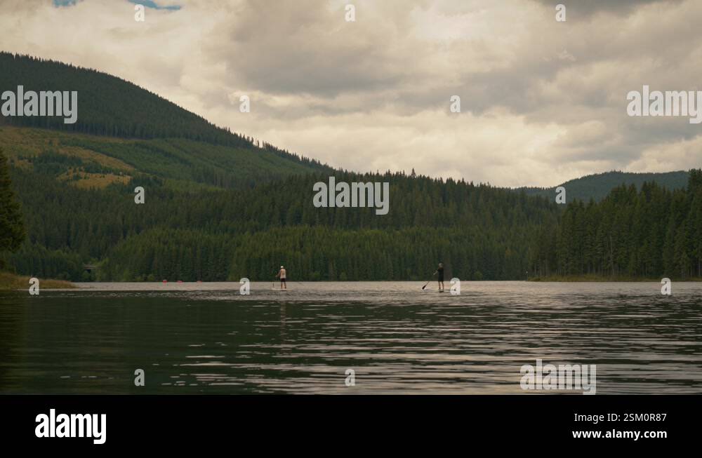 Two men standing on stand up paddle board sup water sport on a mountain ...