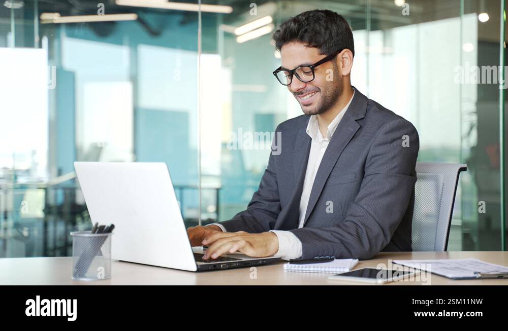 Young businessman in a formal suit typing on a laptop while sitting at ...