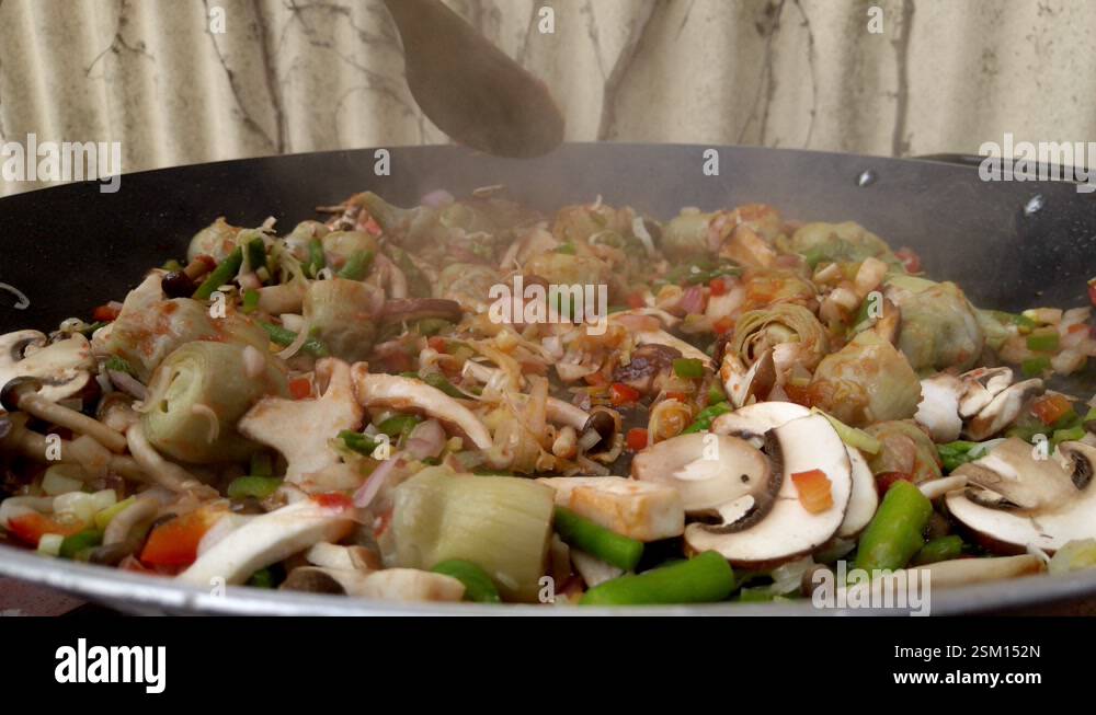 Wooden spoon moving food across hot pan on a stove. Frying food safely ...