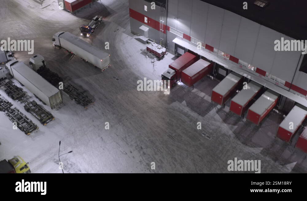 Aerial view of a semi-trailers trucks maneuvers along a warehouses with ...