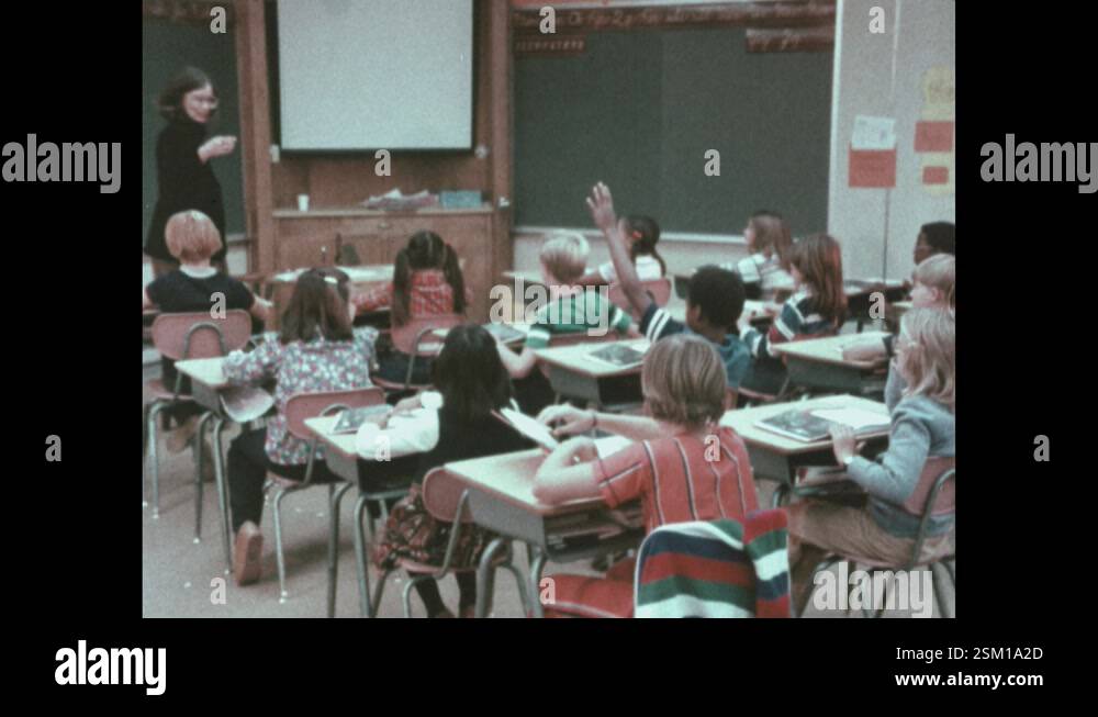1970s: teacher puts book on student's desk in classroom, calls on ...