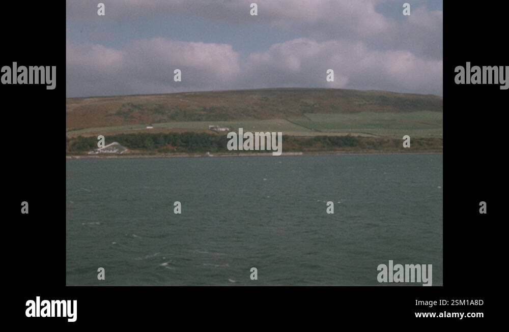 1960s: Choppy waters off of green rolling hills. One home on the shore ...