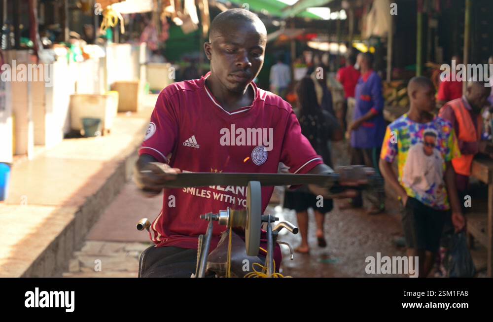 African grinder sharpening long blade on grinding wheel while pedaling ...