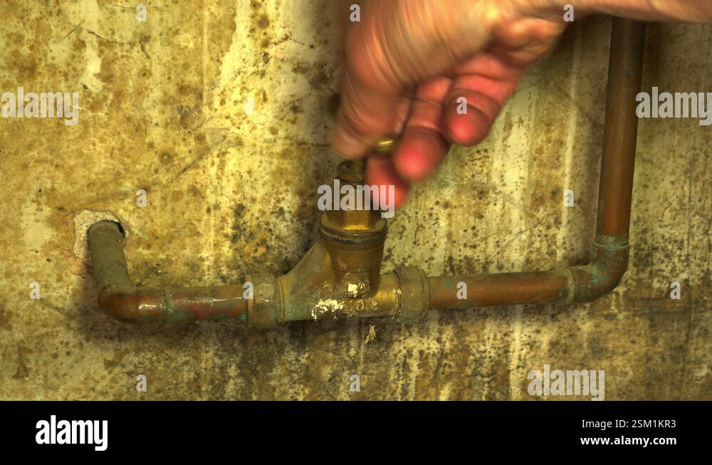 A man's hand turning on a water tap or faucet, attached to a dirty ...