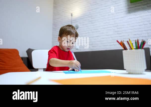 Talkative Caucasian toddler sitting at the desk draws with a pen ...