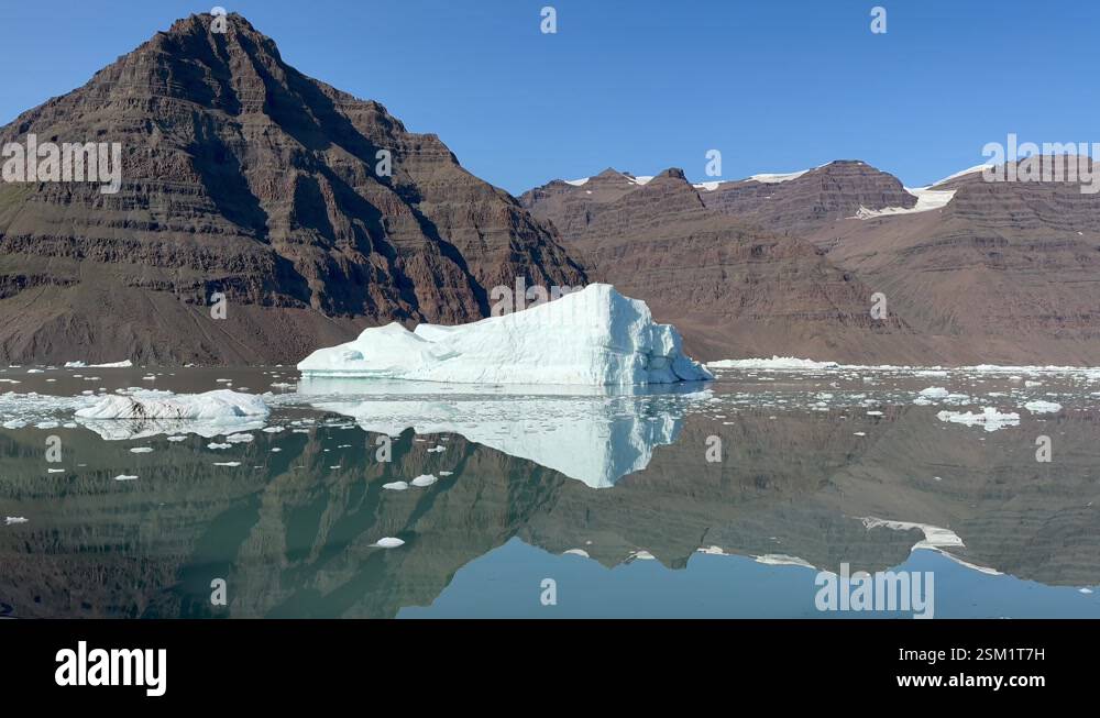 Small iceberg floating by in the mirror-smooth water in Vikingebugt ...