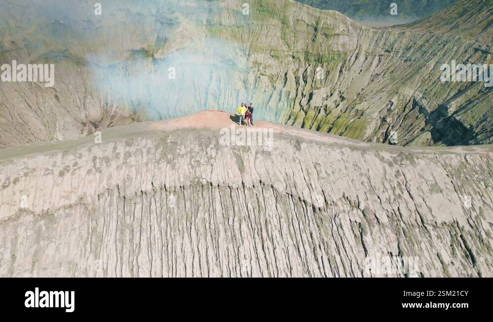 Family of travelers stands at the edge of a crater of active volcano ...