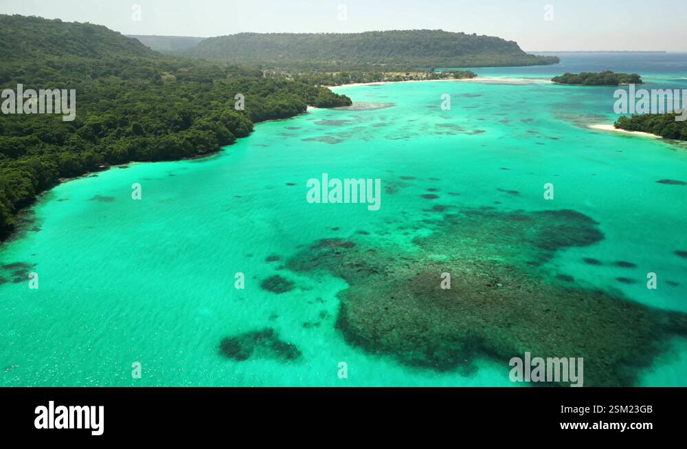 A drone flies over crystal clear waters and the village of Port Olry on ...