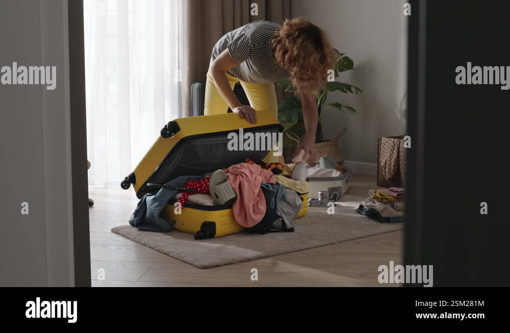 Mess before departure, woman shoves clothes into suitcase, dropping ...