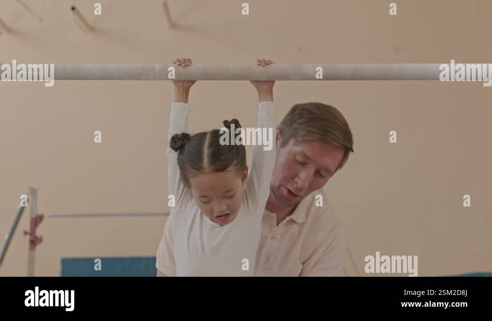 Male Coach Helping Little Gymnast Girl to Do Pull Ups on Bar Stock ...