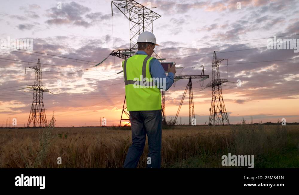 Engineer touches screen of tablet walking past power transmission lines ...