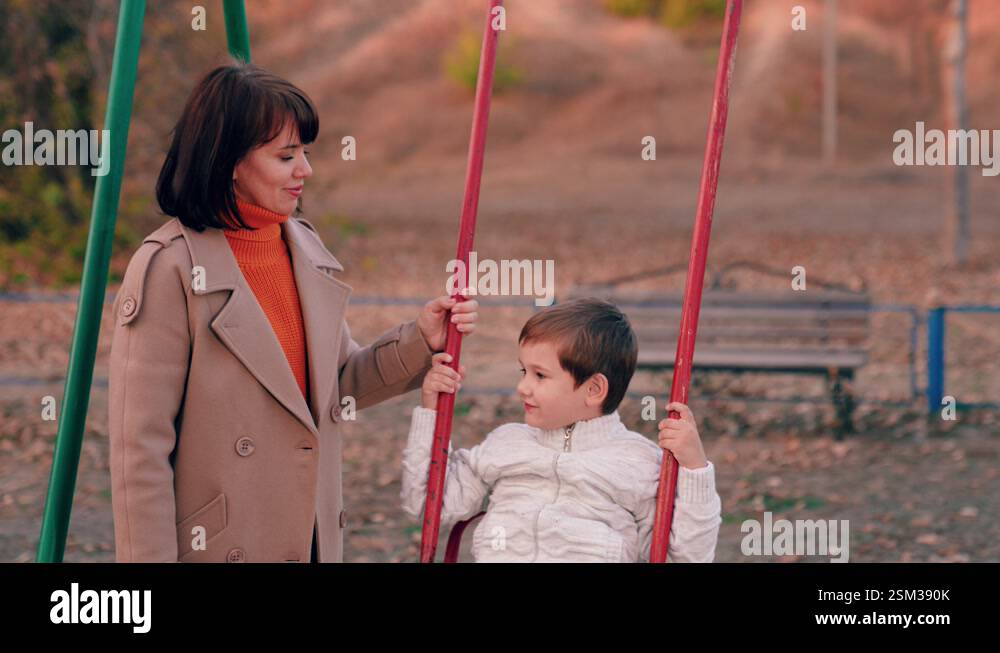 Happy family. Little son sitting on swing smiling, mom rocking child on ...