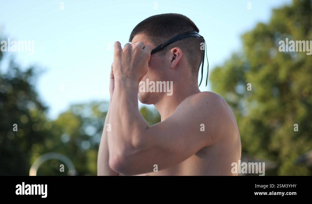 Young attractive swimmer puts on his swimming goggles side profile ...