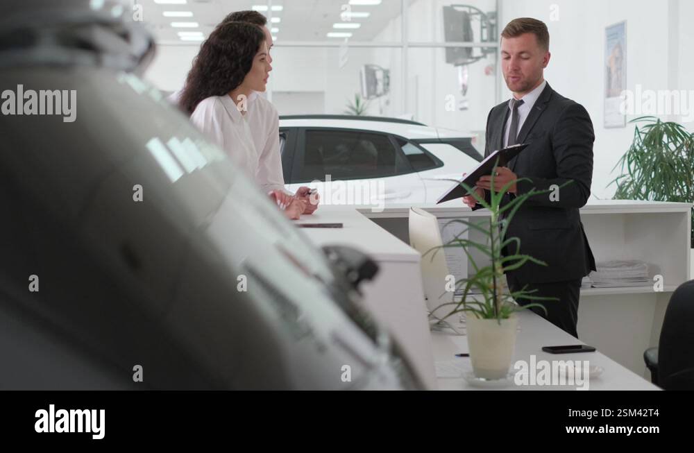 A young family buys a new car at a car dealership, stands at the ...