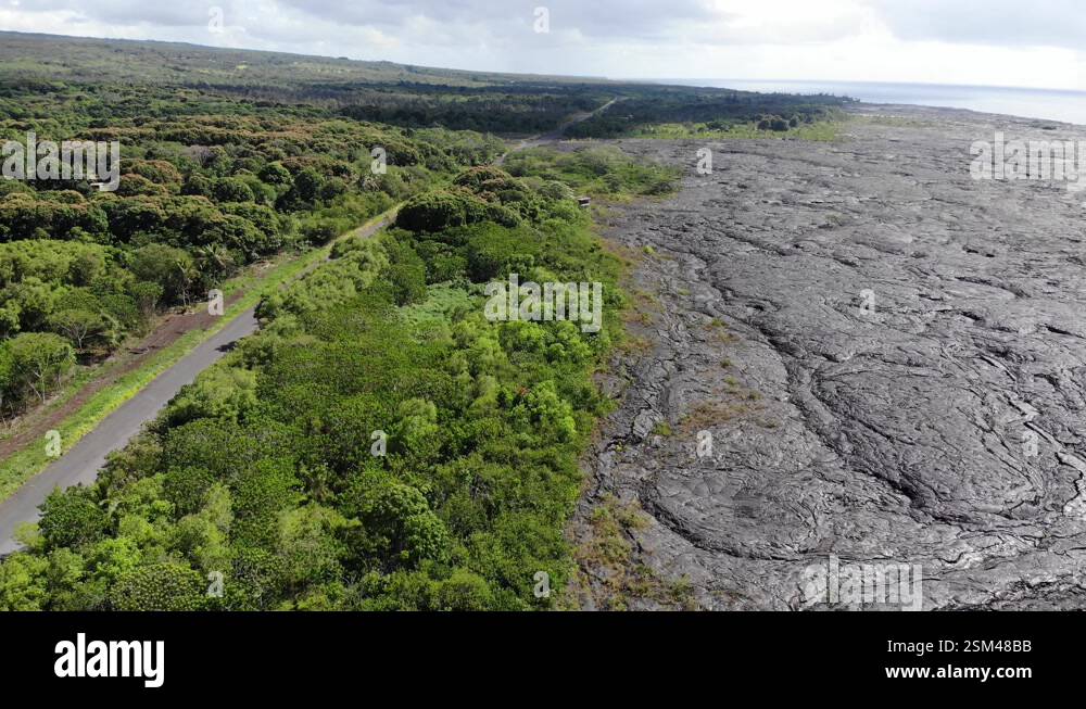 Flying over volcanic flows next to hawaii jungle with a road running ...