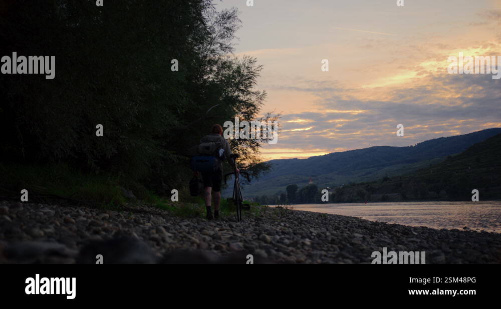 Man walks away with backpack and bikepacking gear across pebble beach ...