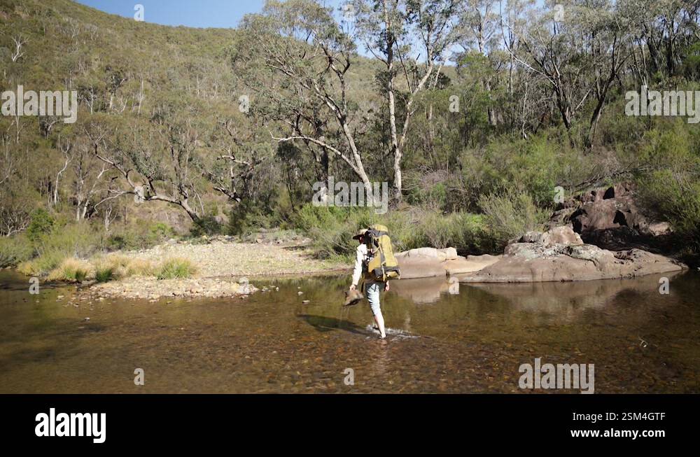 A hiker walks accross a river with a pack on the Victorian High country ...