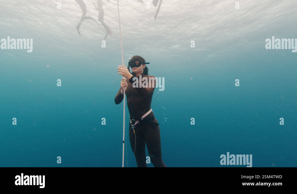 Confident woman freediver ascends along the rope during free diving ...