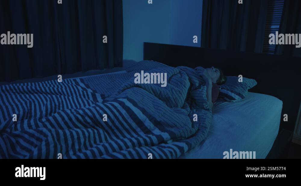 Dolly in of woman sleeping and turning in her bed in a dark bedroom ...