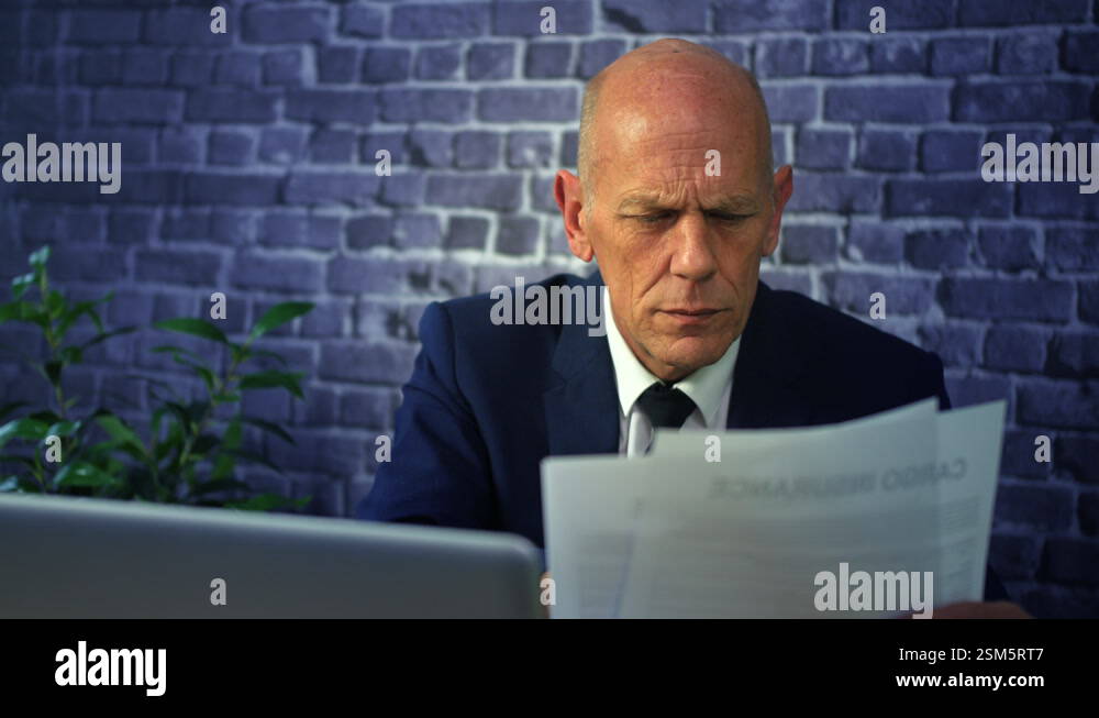 A business man CEO working on a computer looking at paperwork inputting ...