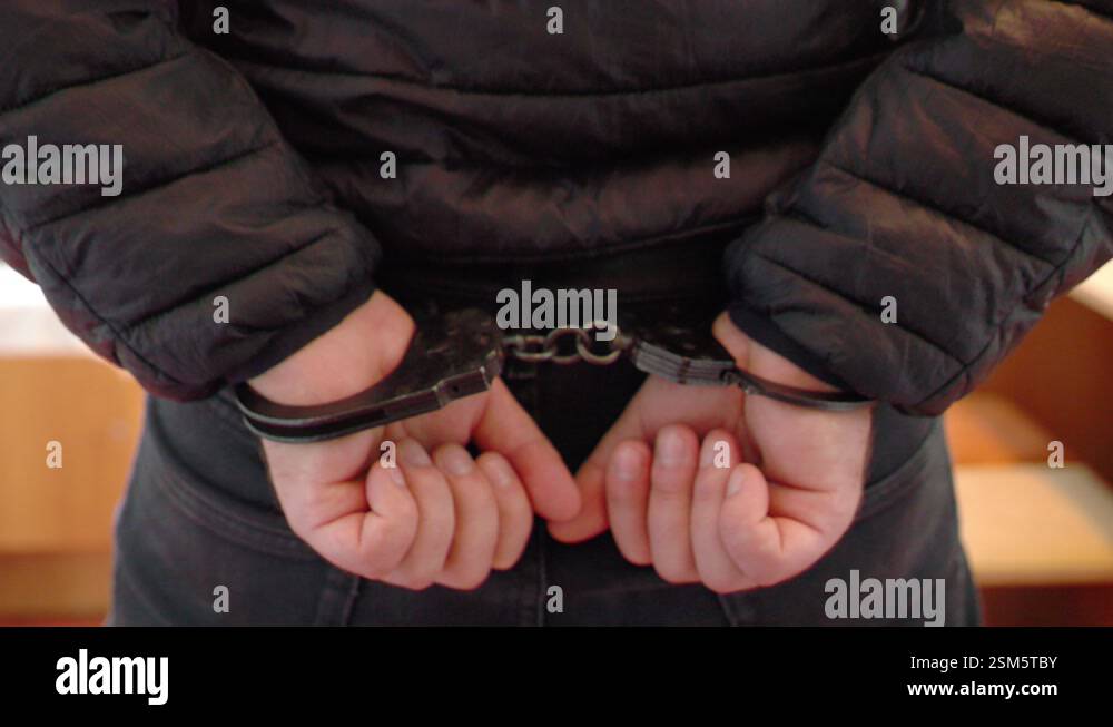 Back view at arrested criminal in cuffs standing in isolated prison ...