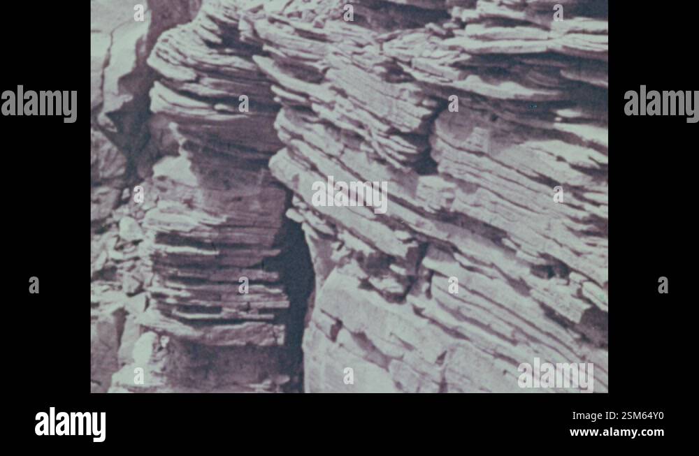 1960s: Layers of rock on various cliff faces. Man examining a rock face ...