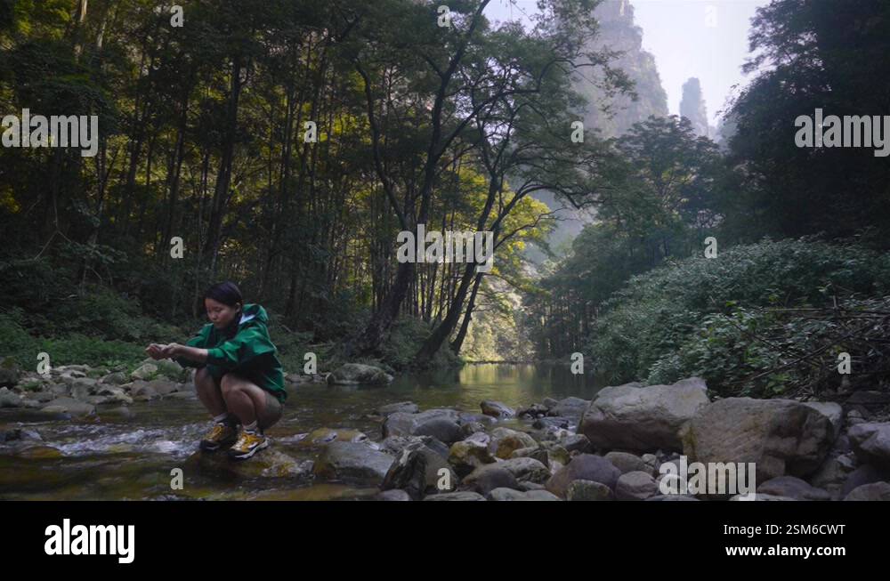 Young asian woman catching water from a clear river in Zhangjiajie ...