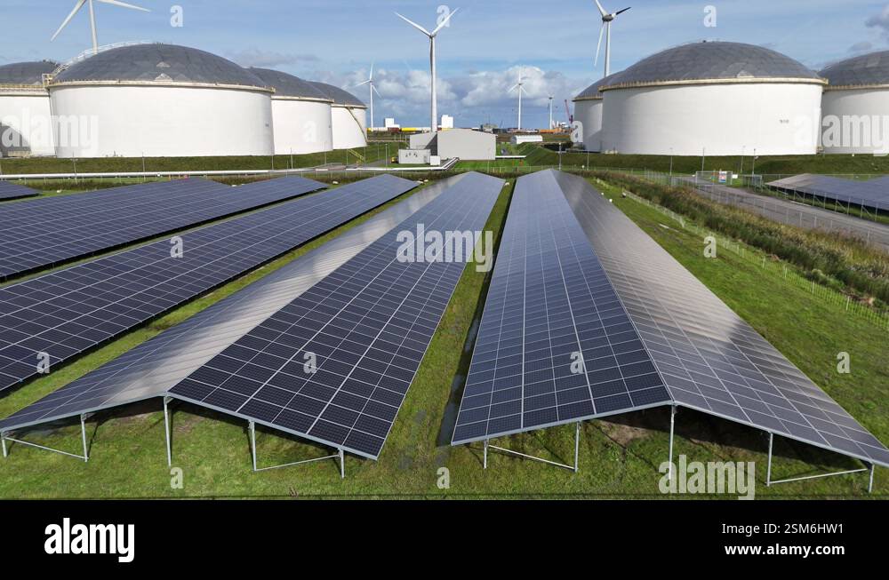 Solar panel park with windmills and fuel silos and harbor in background ...