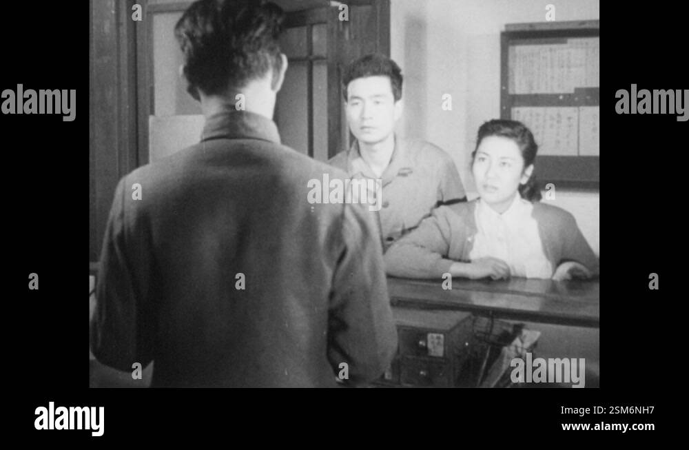 1950s: Couple standing behind the office counter. Man speaking ...