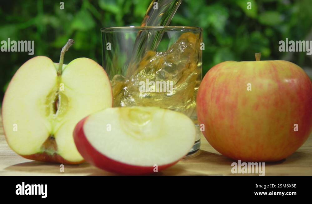 Apple juice is poured in a glass next to large ripe apples cut into ...