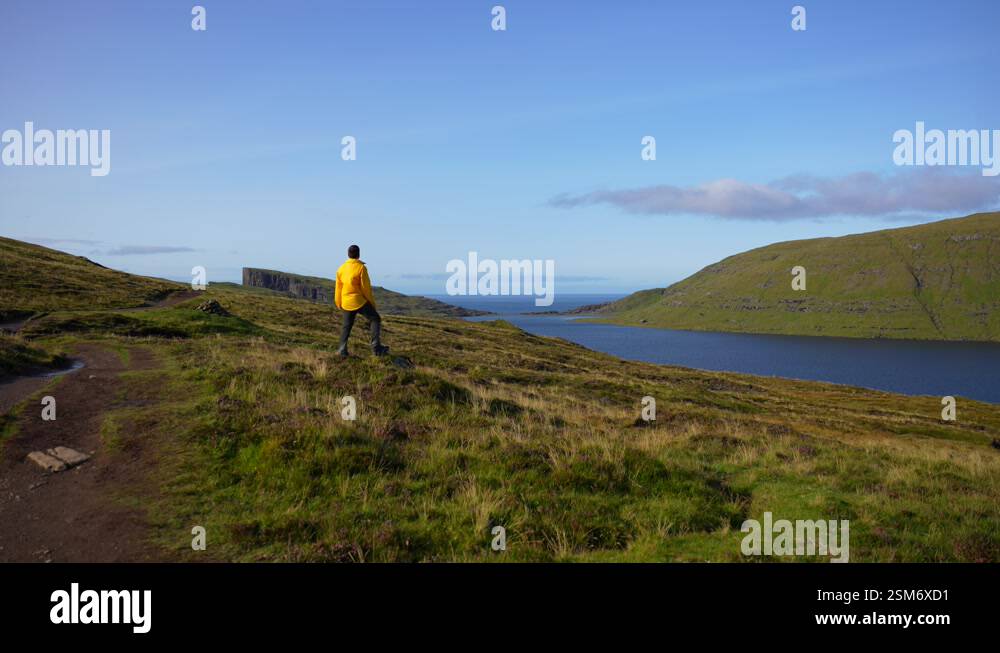 Man in yellow raincoat admiring the green and volcanic Faroese ...