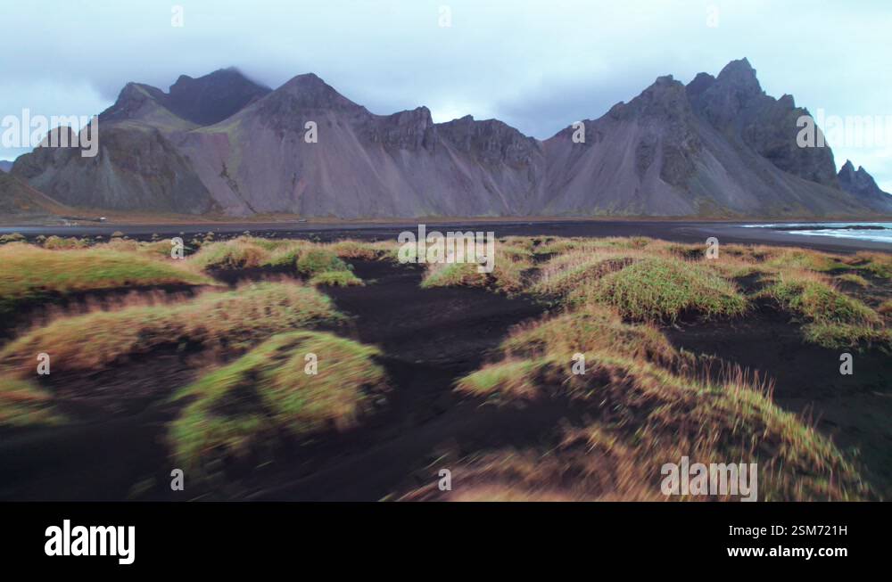 Aerial: Low altitude flight over tussocks toward Vestrahorn, with its ...